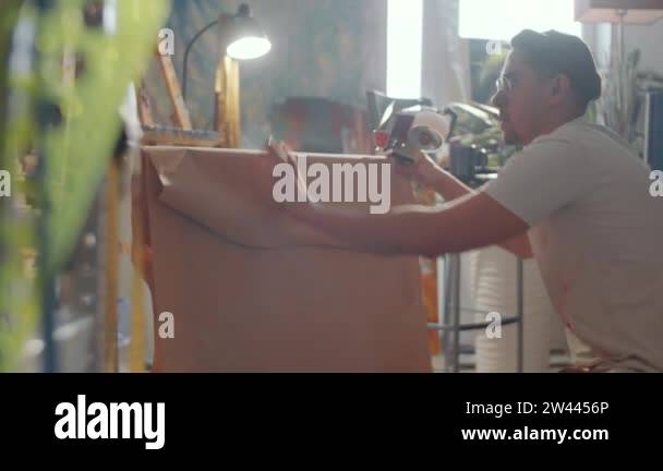 Professional male painter using adhesive tape dispenser while packing ...