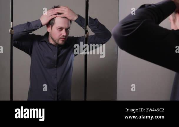 A 35-year-old young man looks in the mirror and touches his hair ...