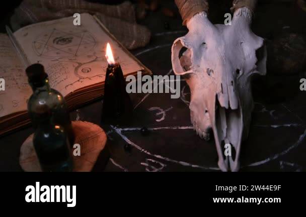 White goat scull with horns, open old book, runes, black candles on ...