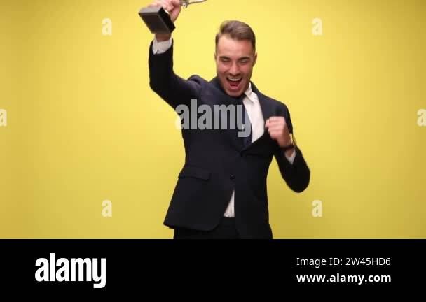 excited young businessman holding trophy, holding arms in the air and ...