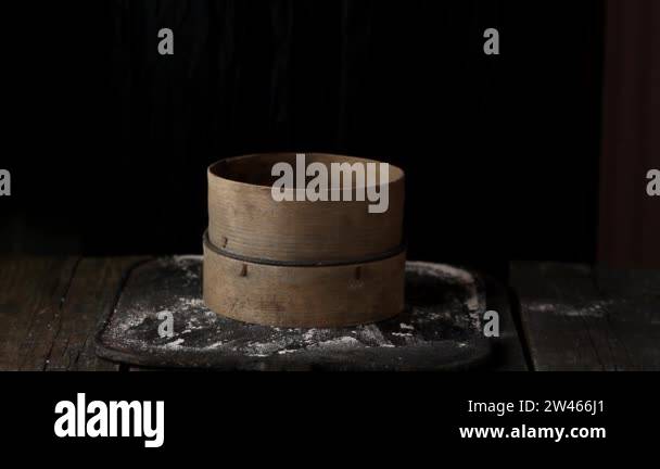 Sieving whole wheat flour through old sieve by woman's hands. Dark ...