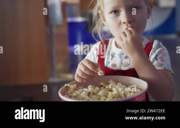 Little girl eats popcorn in movie theater. Media. Cute girl eating ...