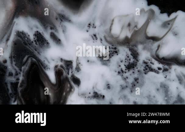 White paint spreads on a black, gold-glittering, moving background ...