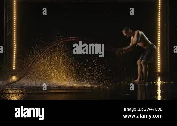 Masculine sportsman doing workout using a battle rope. Side view. The ...