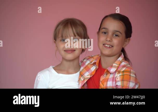 little smiling girls, sisters, best friends hug on a pink background ...
