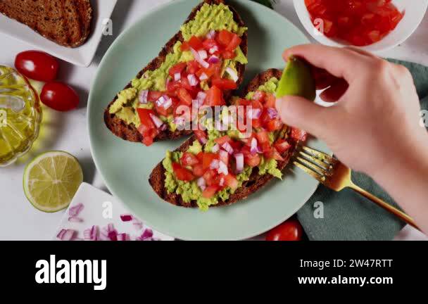 Top view of woman's hand squeezing slice of lime on the top of avocado ...