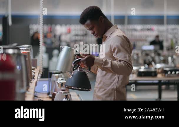 young black man is comparing two electric kettle in store, holding both ...