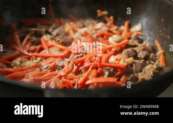 Meat, carrot and onions are stewed in a cauldron in a sauce close-up ...