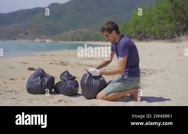 Man in gloves collects plastic trash on a beach. The problem of garbage ...