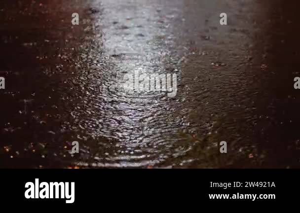 At night Close-up drops of summer or autumn rain fall on the asphalt in ...