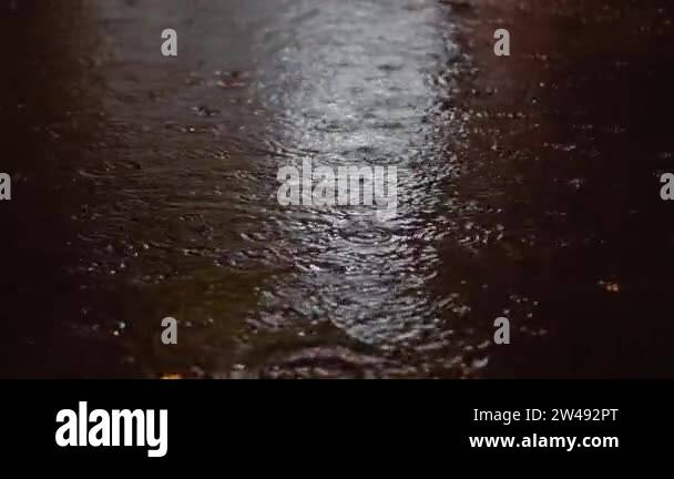 At night Close-up drops of summer or autumn rain fall on the asphalt in ...