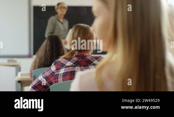 Back view of the kids sitting in the classrom and rising hands to ...