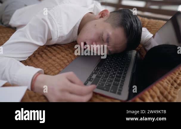 Tired young Chinese man yawning lying on laptop keyboard napping in ...