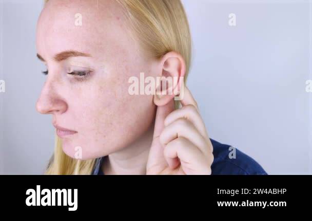 A woman on a white background shows her ear. The macro video shows the ...