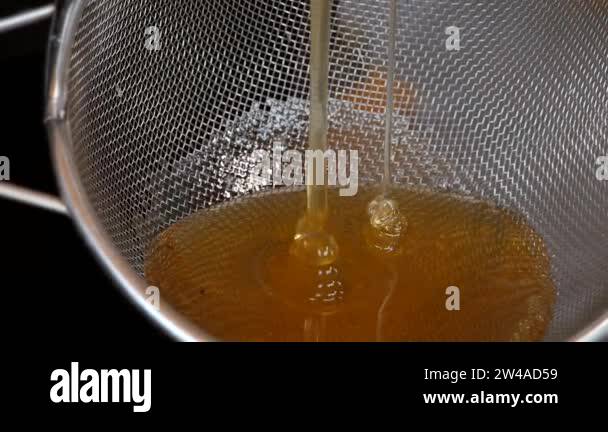 Beekeeper turns the handle of the honey extractor and a stream of honey ...