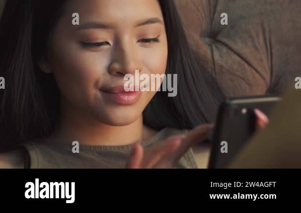 A close-up view of a smiling young asian woman is typing on her ...