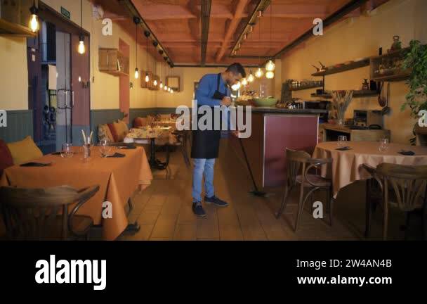 African American waiter sweeping the restaurant dining room floor with ...
