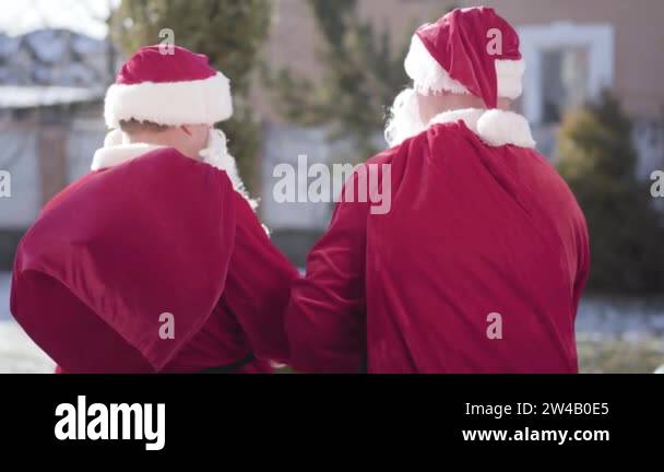 Two Santas in Christmas costumes with gift sacks turning, waving at ...