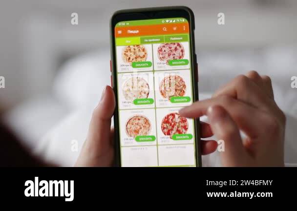 A woman orders fast food online using an application on a smartphone. The girl chooses pizza in ...