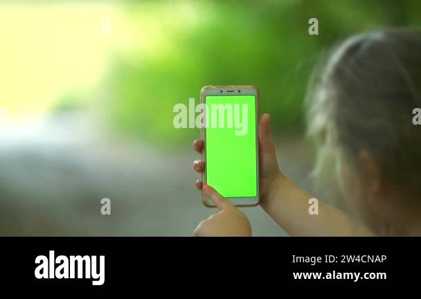 Girl's hand holds smartphone with green screen. Back view shot. Chroma ...
