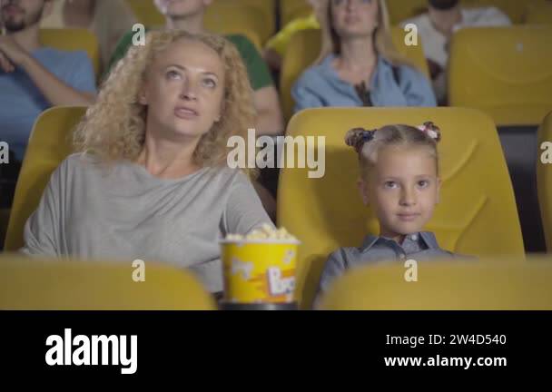 Embarrassed Caucasian mother closing daughters eyes in cinema. Portrait ...