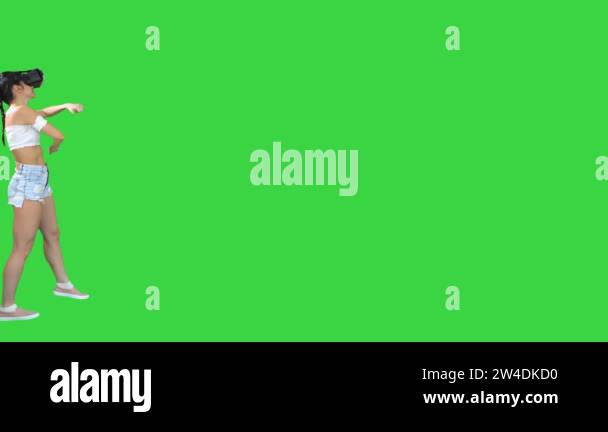 Woman using VR Virtual Reality headset walking and dancing on a Green ...