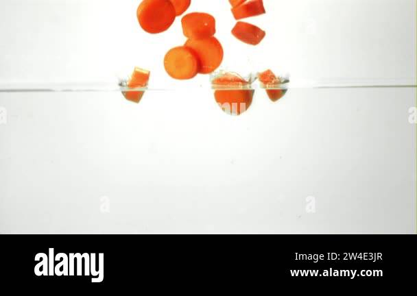 Super slow motion sliced carrots fall into the water with splashes and ...