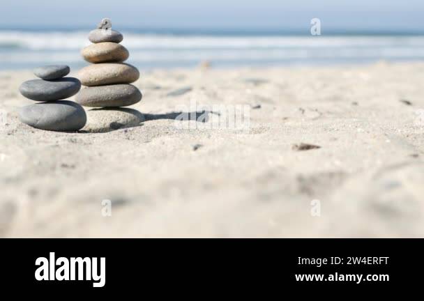 Rock balancing on ocean beach, stones stacking by sea water waves ...