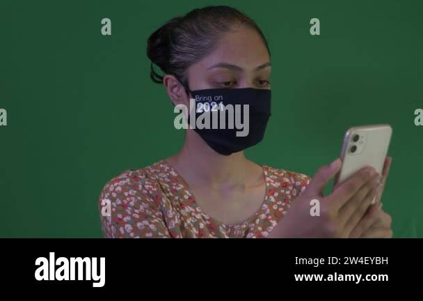 Young Asian Woman Wearing Bring It On 2021 Face Mask Holding Smartphone ...