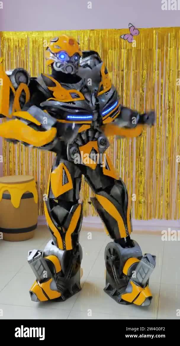 Vertical video. An animator in suit of yellow transformer bumblebee robot model dancing. Man in ...