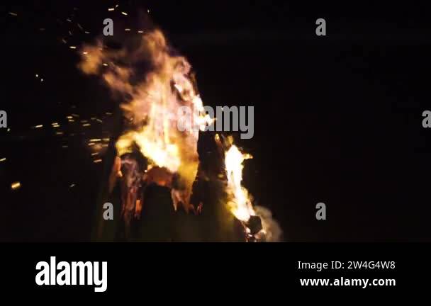 Log fire burns in wind at night, throwing out flames and sparks into ...