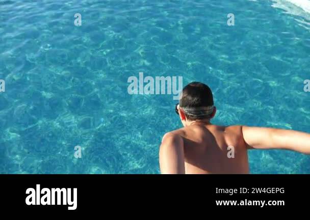 Funny boy jumping feet first in a pool with splashes in summer in slow ...