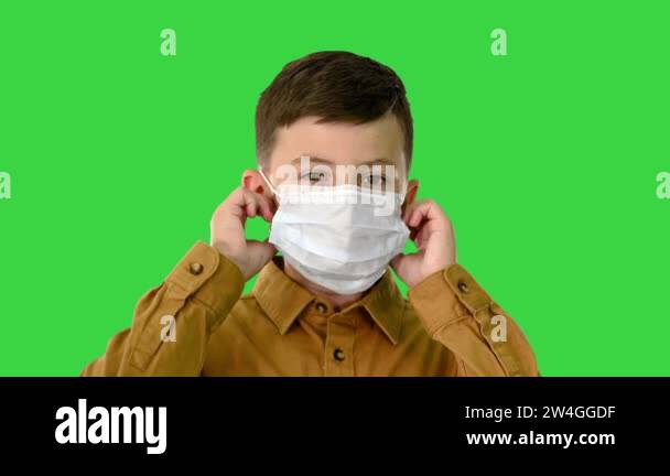 Little boy taking his face mask off and smiling at camera on a Green ...