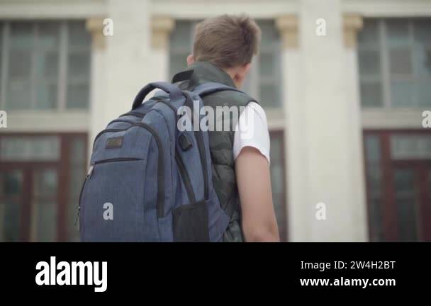 Back view of upset schoolboy standing in front of school and shaking ...