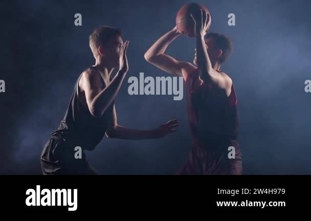 Two young athletes practice basketball in a dark smoky studio under the ...