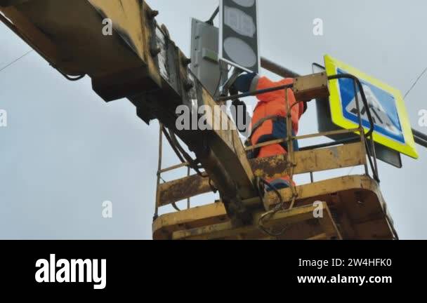 A worker in an elevator cradle repairs an LED traffic light. Road sign ...