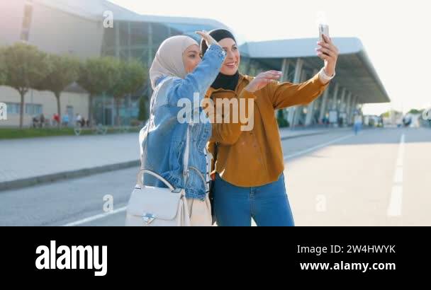 Young Arabian pretty cheerful women in traditional hijabs smiling, waving hand and talking on ...