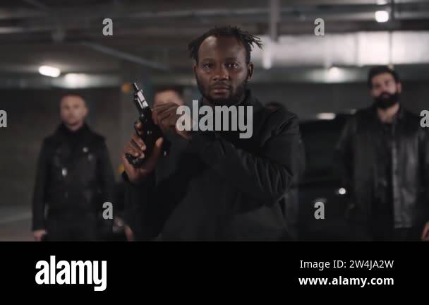 Portrait of brutal African American gangster refreshing gun looking at ...