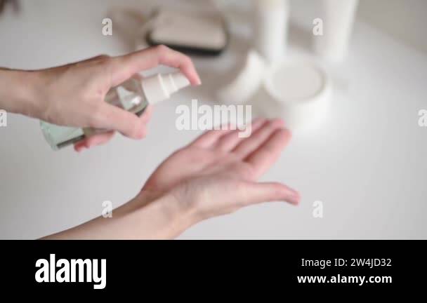 Woman at the table with cosmetics splash antiseptic lotion on her hands ...