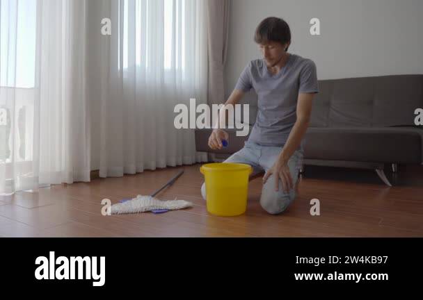 A young man washes floor in an apartment. He puts washing liquid into ...