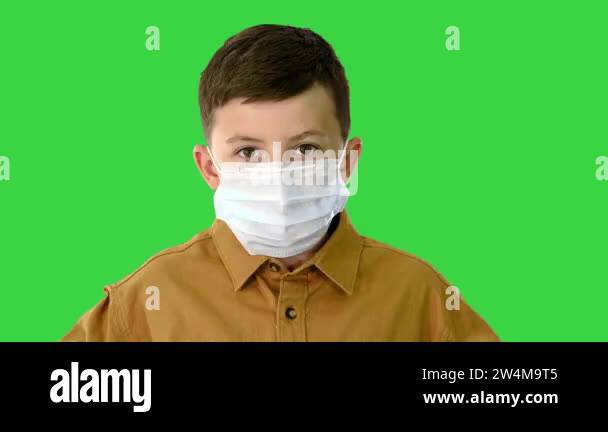 Little boy adjusting his face mask looking at camera on a Green Screen ...