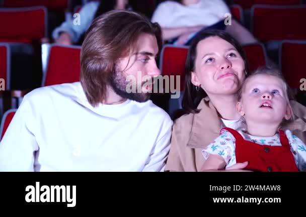 Friendly family watching a movie in the cinema. Media. Young parents ...