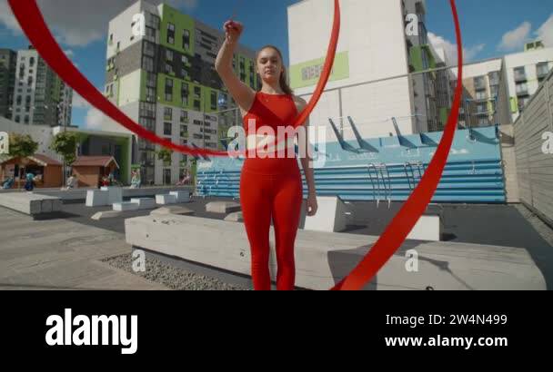 Young woman in red performs callisthenics with ribbon at workout playground outdoors, gymnast ...
