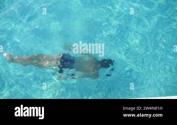 Cheery boy diving and swimming underwater in a wading pool in slow ...