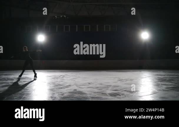 Skaters training on the indoor ice arena in the dark with spotlights ...