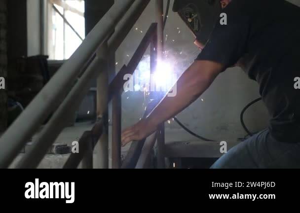 Young worker keeping arc welding device making handrails in a workshop ...