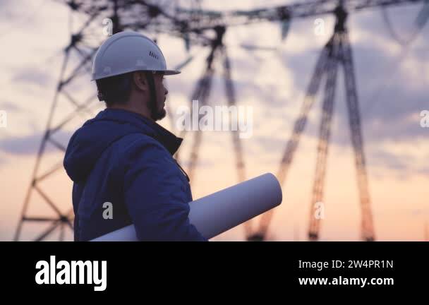 An electrician on the background of high towers of power plants looks ...