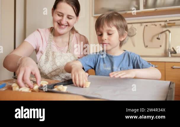 Smiling boy with mother making biscuits and putting them on baking ...