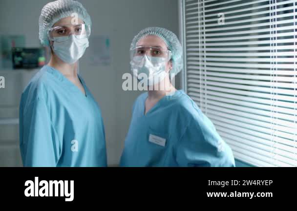 Two young female nurses in protective masks, glasses, sterile hats and ...