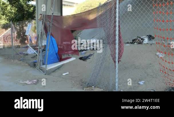 Hole in a fence leading to a homeless encampment under a bridge Stock ...